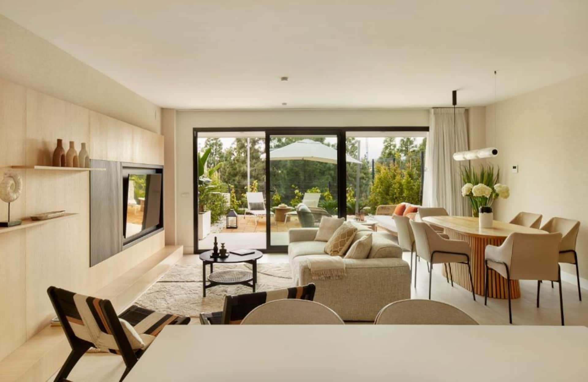 Uma sala de estar moderna com sofá, mesa de jantar e cadeiras, lareira e vista para o exterior através de grandes portas deslizantes.