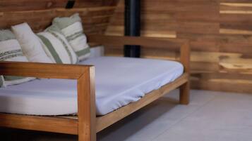 Uma cama de madeira com colchão e almofadas brancas, diante de uma parede de madeira e piso de azulejos.