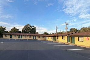 Um motel com uma fileira de quartos, estacionamento e céu azul.