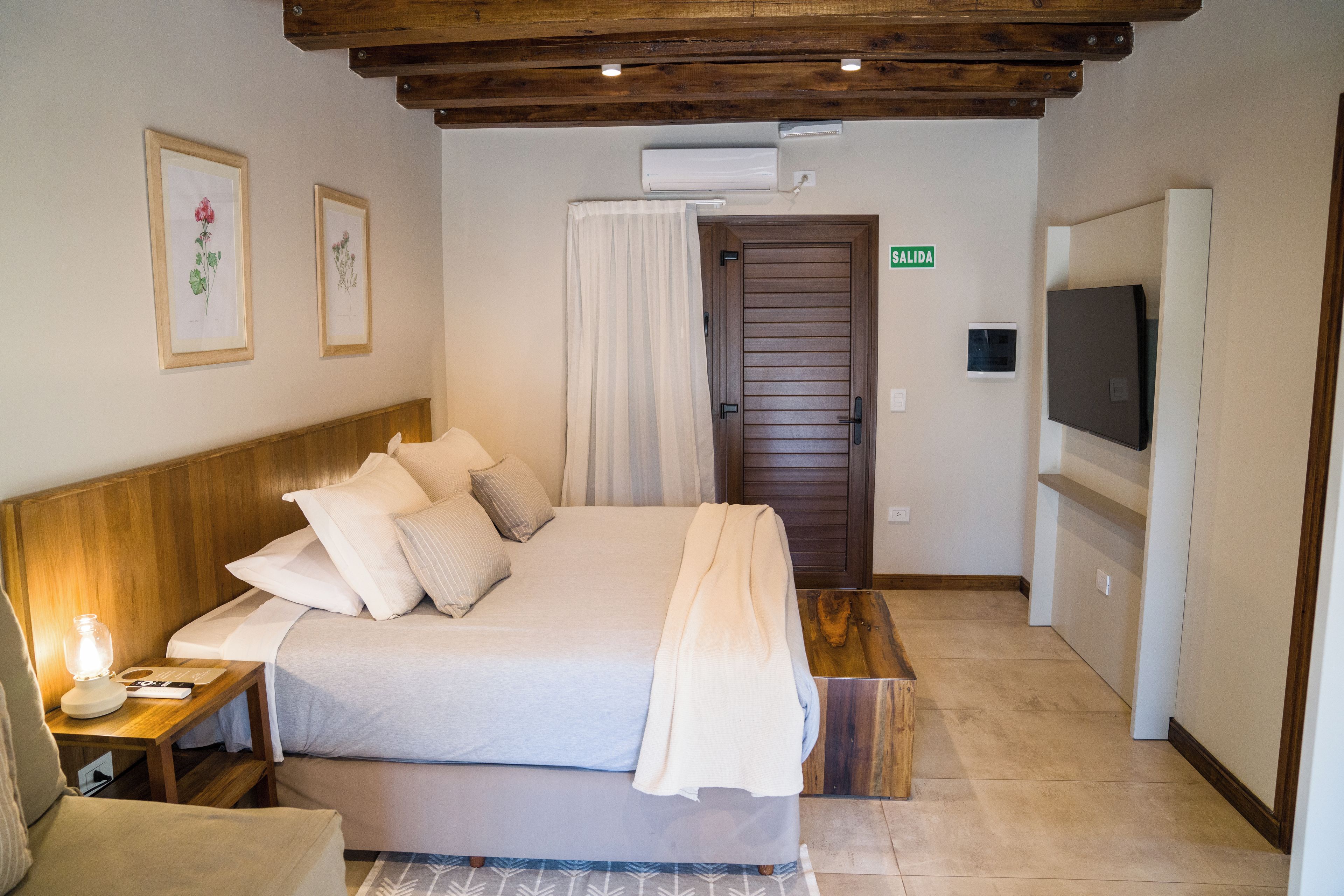 Quarto de hotel com uma cama, mesa de cabeceira, televisão e porta com uma placa.