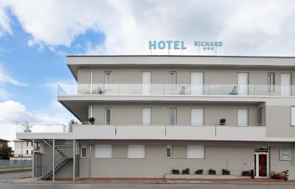 Edifício de hotel de dois andares com fachada plana, varanda no andar superior e porta vermelha na entrada.