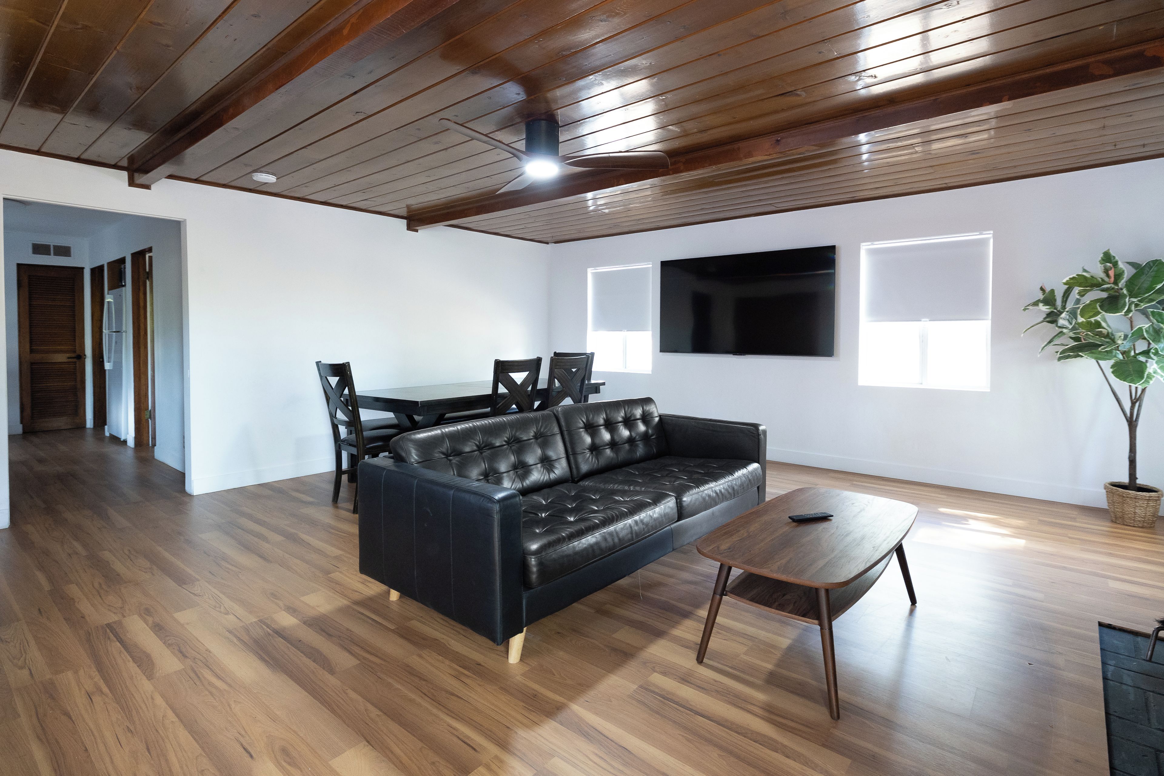 Uma sala de estar moderna com um sofá de couro, mesa de centro de madeira e TV de tela plana na parede.