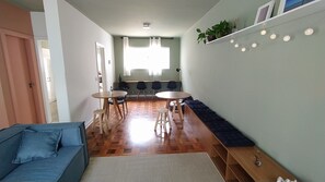 Uma sala de estar com sofá, mesa de jantar com cadeiras, um banco e prateleira na parede com plantas.