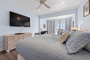 Quarto com cama, penteadeira, televisão e vista para o exterior.