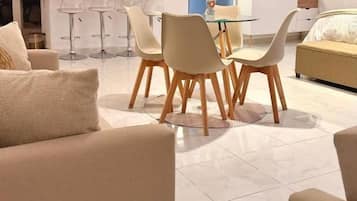 Uma sala de estar moderna com sofá, mesa de jantar com cadeiras e área de cozinha com parede de pedra e banquetas.