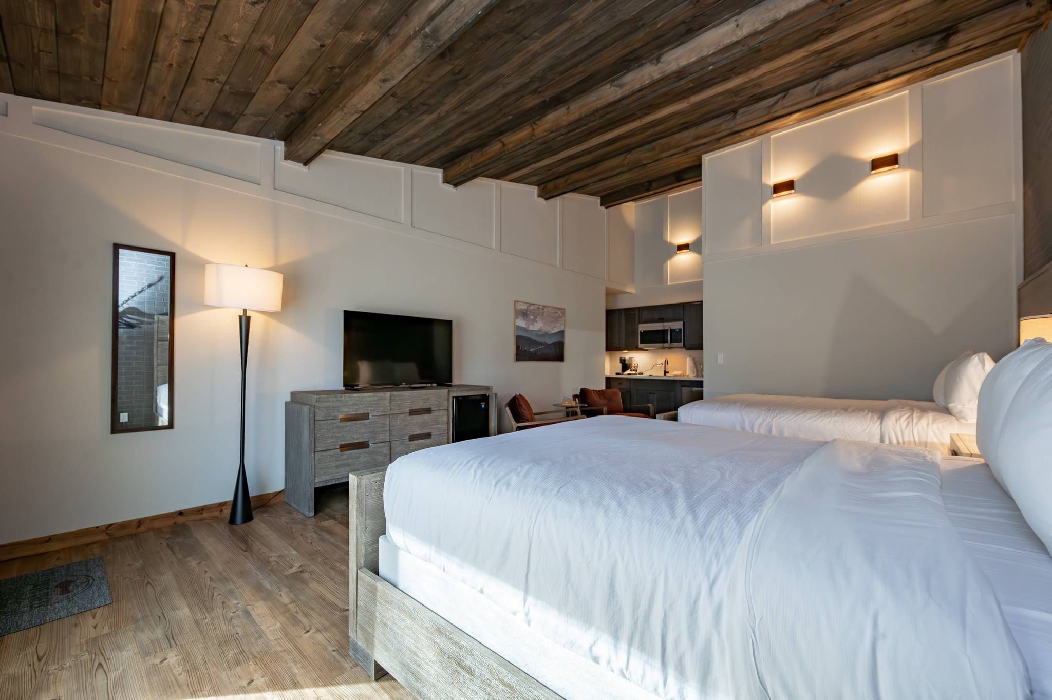 Quarto com cama grande, televisão, escrivaninha e cozinha compacta.