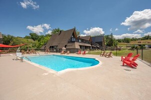 Piscina com espreguiçadeiras, um edifício com telhado inclinado e céu claro.