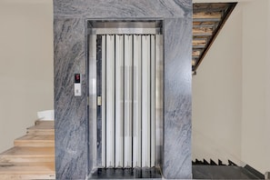 Um elevador com painel digital, interior metálico e parede de mármore.
