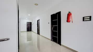 Um corredor com um extintor preso na parede, uma porta com uma placa e chão de azulejos.