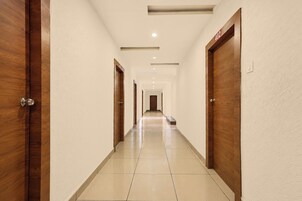 Corredor de hotel com portas de madeira, paredes brancas e chão de azulejos.