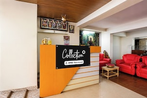Uma área de recepção com uma placa indicando 'Collector' e 'OYO-Serviced'. Há um balcão de madeira, um sofá vermelho e uma pequena mesa com uma tigela. O quarto tem teto de madeira e piso de azulejos.
