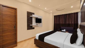 Quarto de hotel moderno com guarda-roupa de madeira, cama com colcha preta e branca, televisão montada e sofá de cor escura.