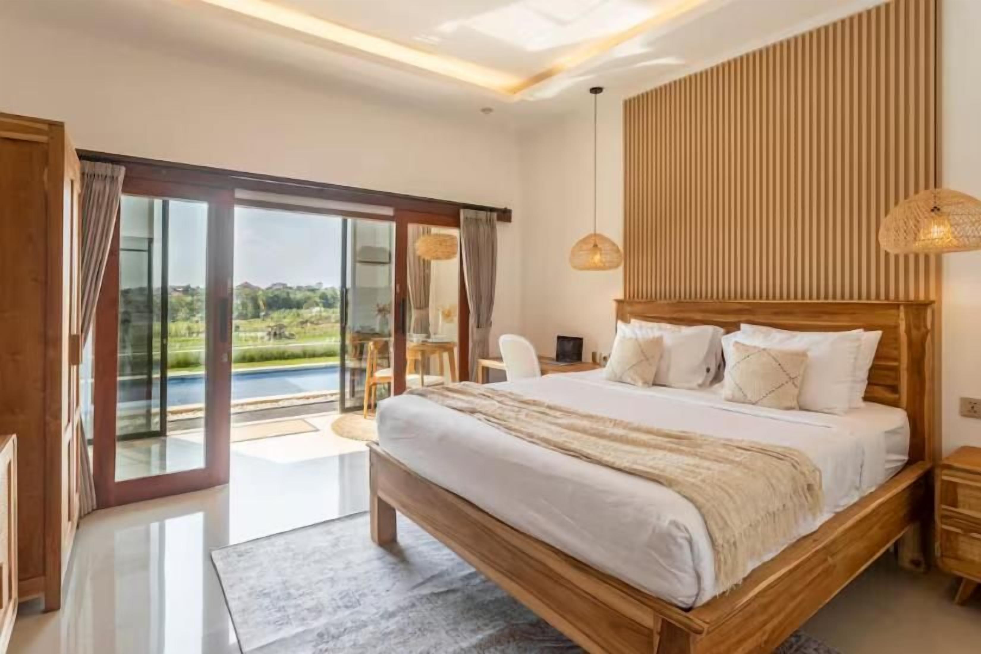 Quarto com uma cama grande, porta de vidro deslizante para uma varanda e cabeceira de madeira.