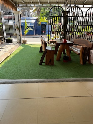 Espaço ao ar livre com mesas e cadeiras, um caixa eletrônico e entrada com portão.