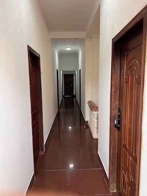 Um corredor com piso de azulejos polidos, portas de madeira e luminária no teto.