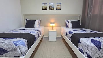 Quarto de hotel com duas camas de solteiro, mesa de cabeceira com abajur e três quadros na parede.