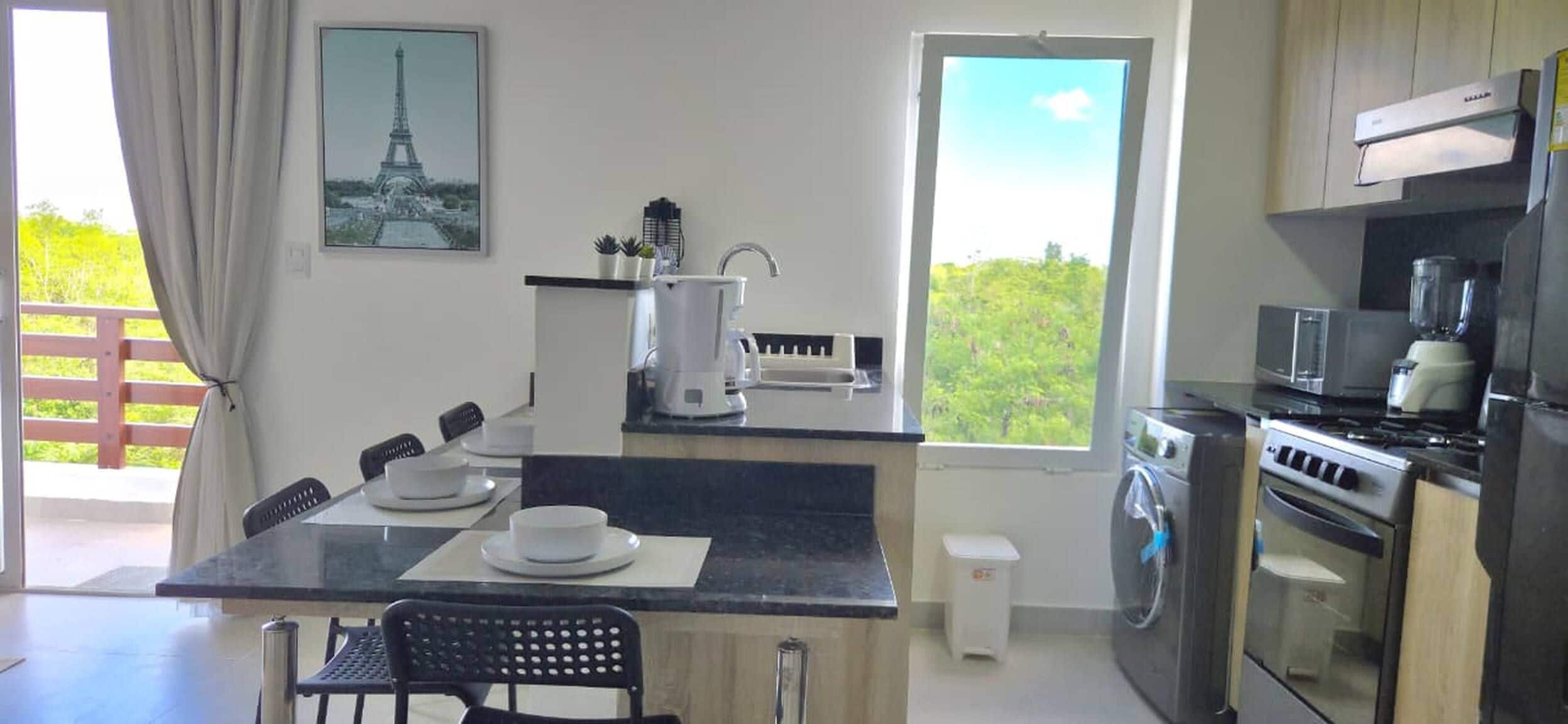 Cozinha compacta com área de refeições, cafeteira, micro-ondas, fogão e máquina de lavar roupa.