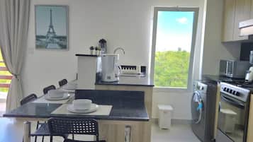Cozinha compacta com área de refeições, cafeteira, micro-ondas, fogão e máquina de lavar roupa.