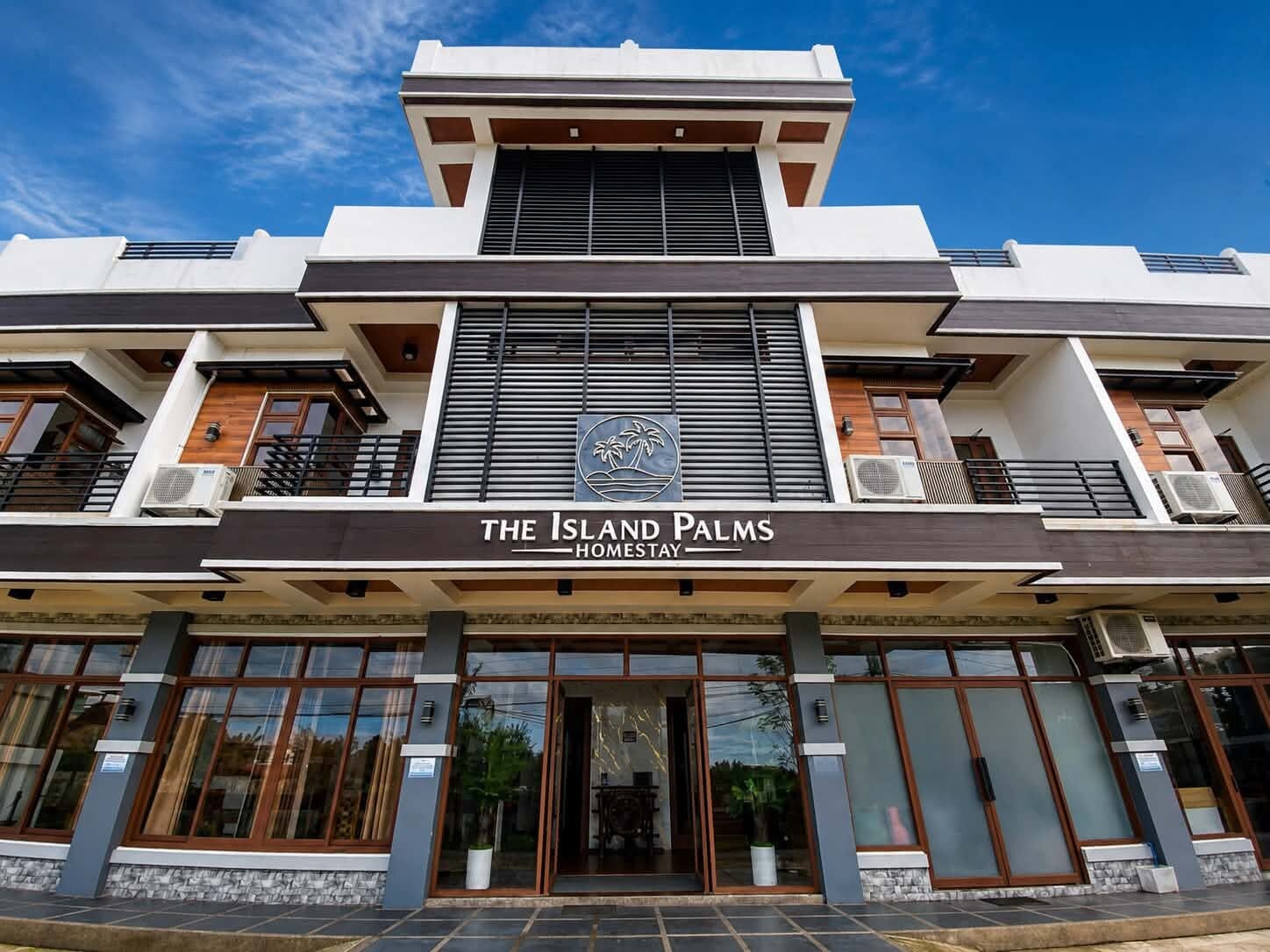 Um hotel moderno com um logotipo em destaque, grandes janelas e unidades de ar condicionado.