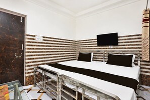 Quarto de hotel com cama, televisão fixada na parede e porta com puxador.