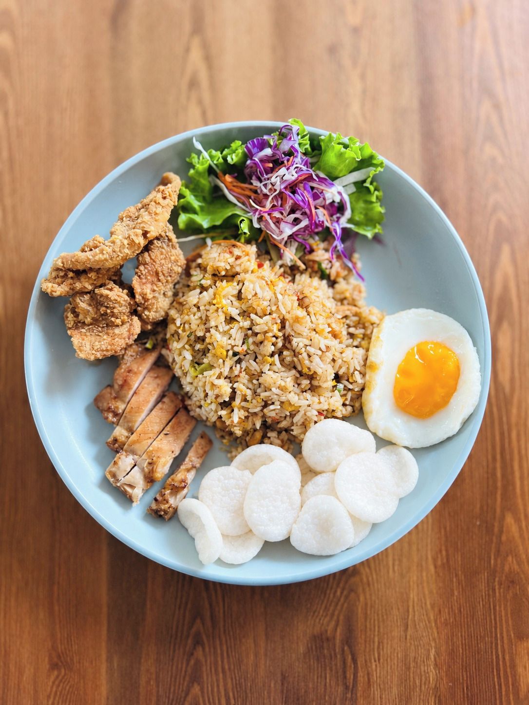 Um prato de arroz frito, carne fatiada, frango frito, um ovo frito e uma salada.