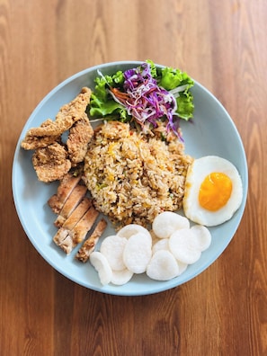 Um prato de arroz frito, carne fatiada, frango frito, um ovo frito e uma salada.