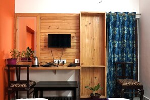 Quarto compacto com televisão de parede em madeira, uma mesinha com chaleira, um banco e uma cadeira.