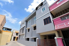 Edifício residencial de vários andares com fachada plana, entrada protegida por portão e céu claro.
