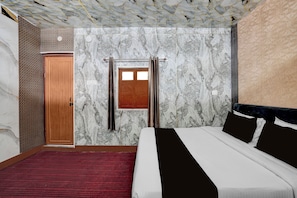Quarto de hotel com parede estampada em mármore, porta de madeira, cama com roupa de cama preta e branca e tapete vermelho.