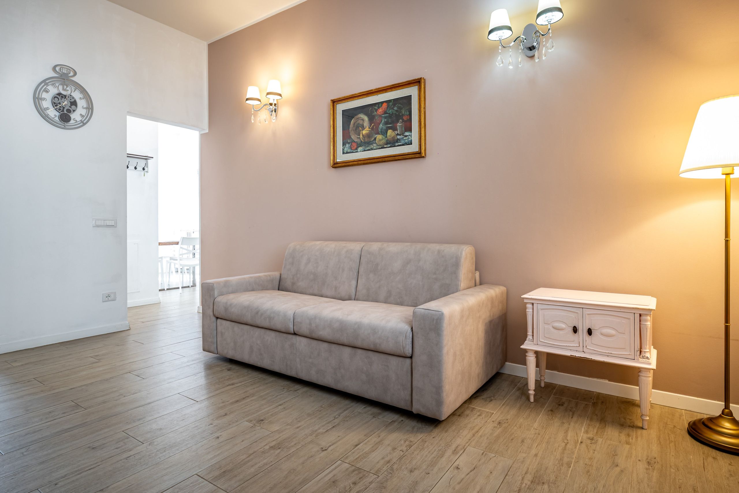 Uma sala de estar moderna com um sofá bege, uma mesinha de apoio branca, um quadro pendurado na parede e um abajur.