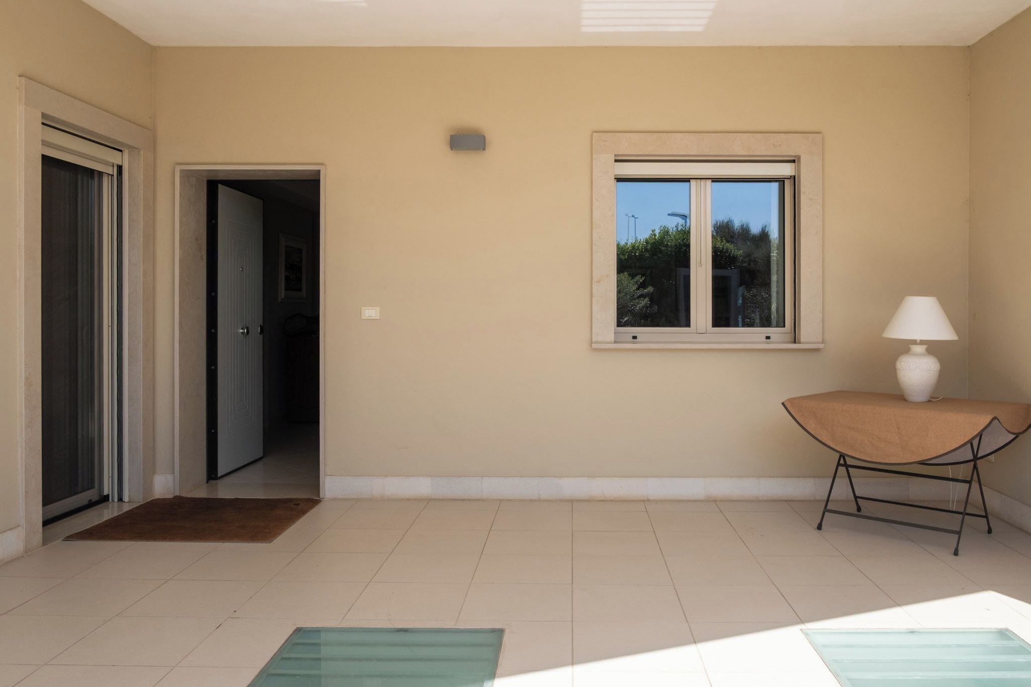Um quarto com porta, janela, luminária e uma cadeira.
