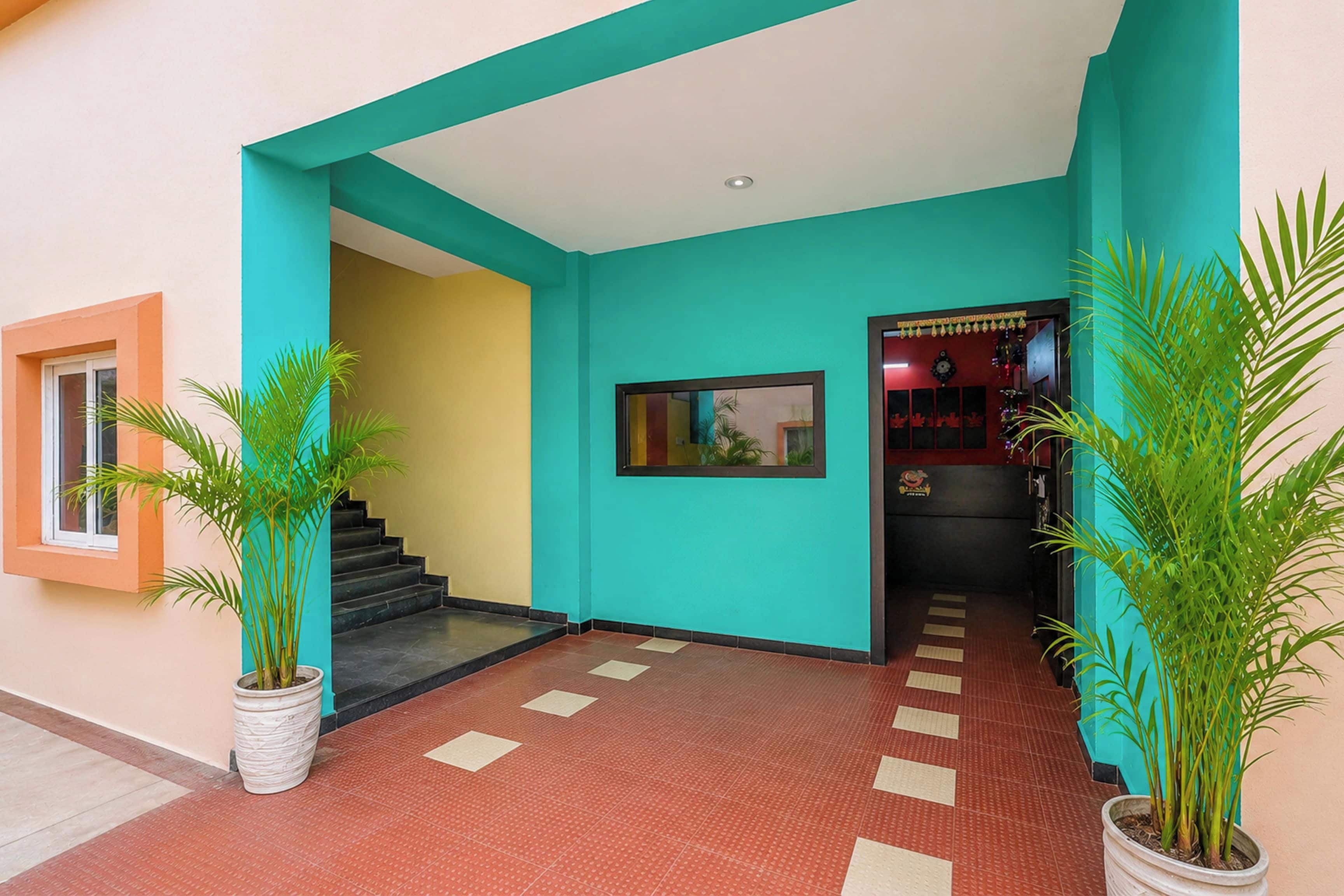 Entrada de hotel com parede azul-turquesa, escadaria e plantas em vasos.
