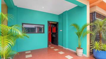 Corredor com paredes verde-água, uma porta vermelha e plantas em vasos.