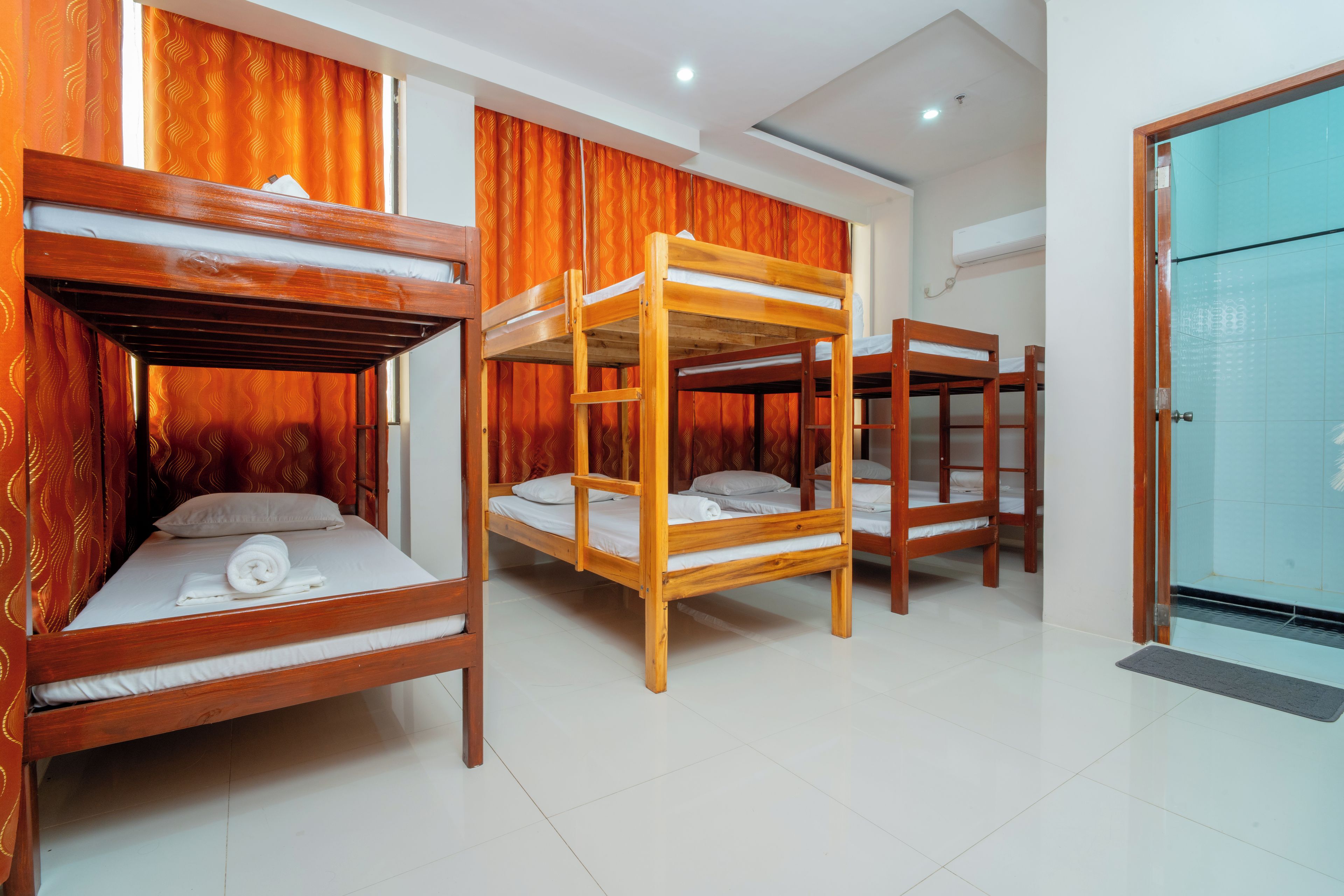 Um quarto com três beliches de madeira, cortinas com padrão laranja e piso de azulejos.