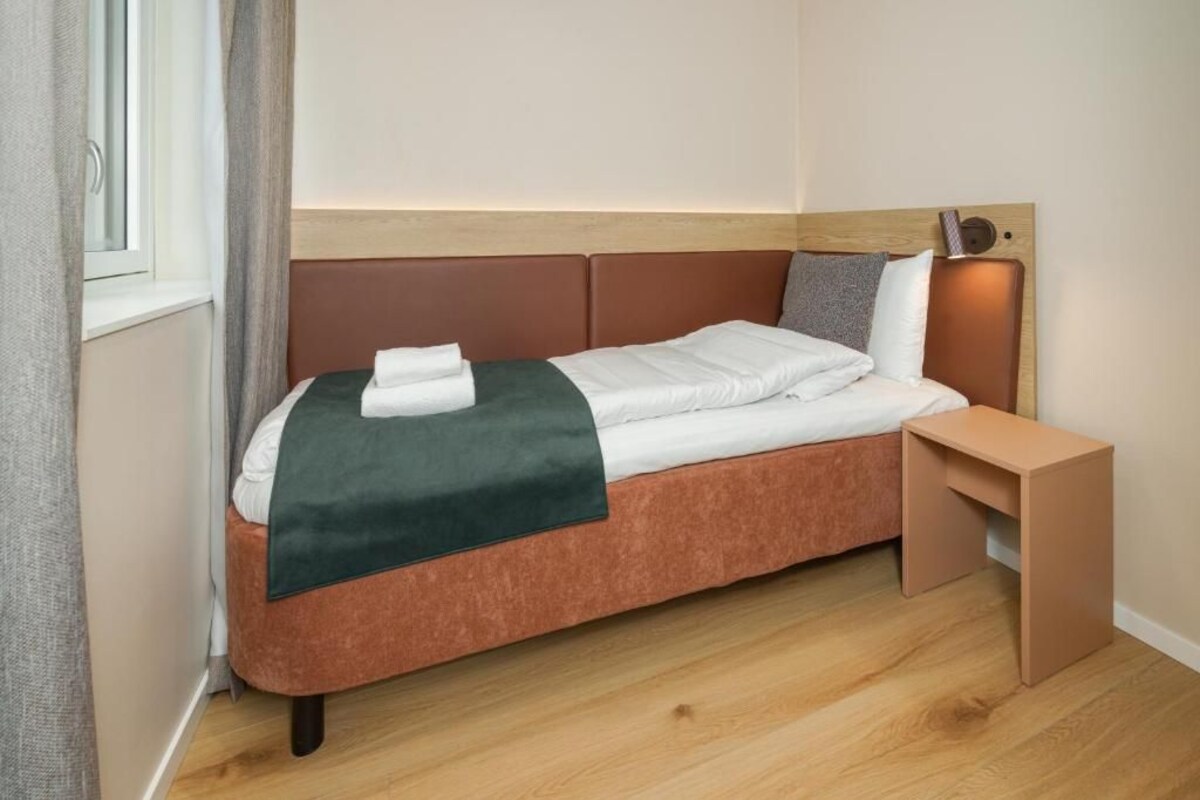 Uma cama de solteiro com cabeceira, mesa de cabeceira e janela com cortinas.
