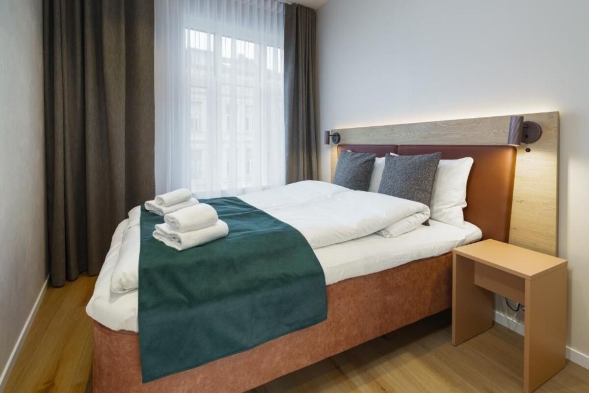 Quarto de hotel com cama, mesa de cabeceira e vista da cidade pela janela.