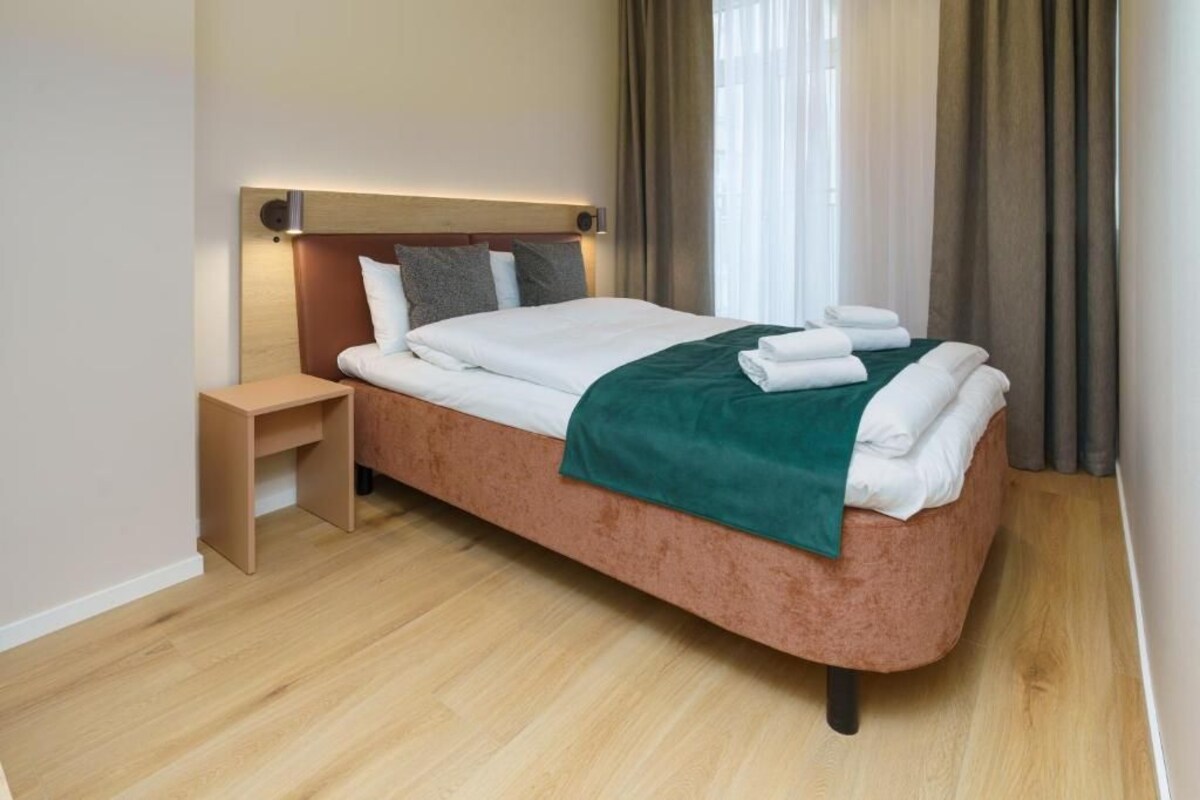 Cama bem arrumada com cabeceira, mesa de cabeceira e manta verde.