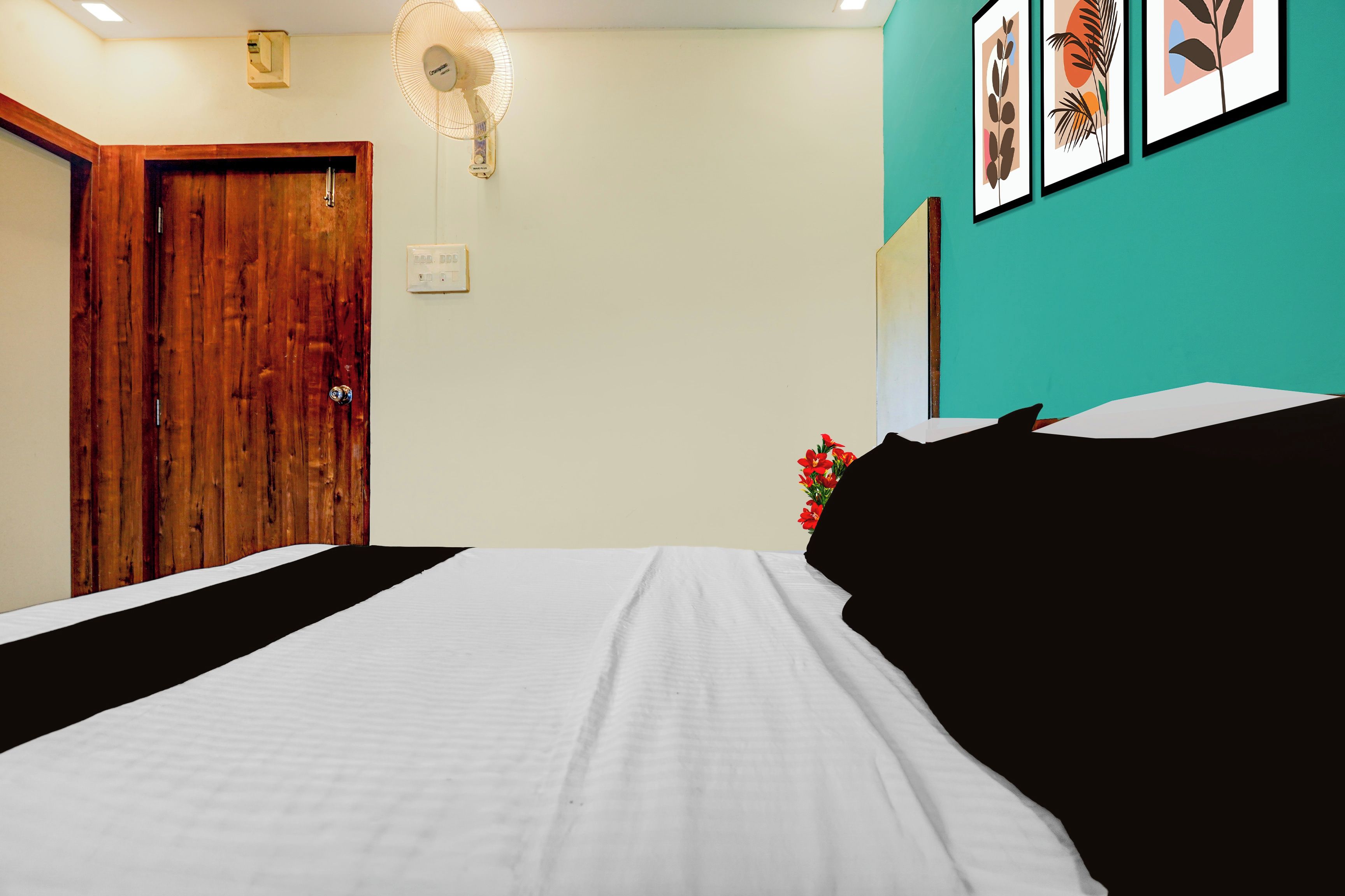 Quarto com porta de madeira, ventoinha na parede e cama com roupa de cama preta e branca.