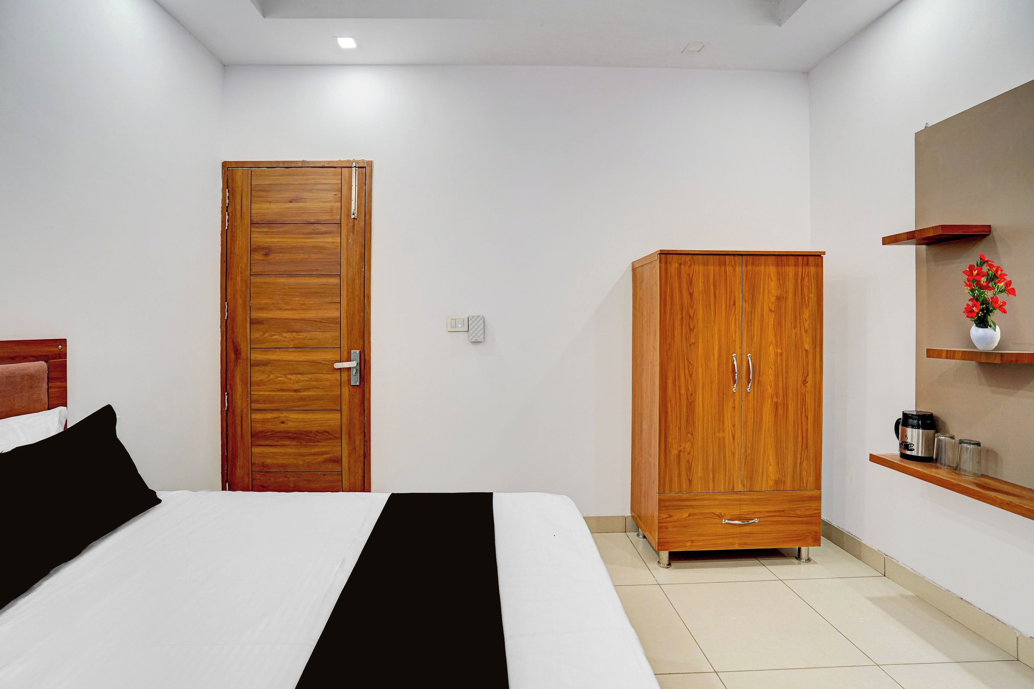 Quarto de hotel com cama, guarda-roupa, estante com um vaso e máquina de café.