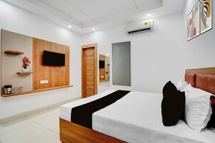 Quarto de hotel moderno com cama, TV montada na parede, ar-condicionado fixado na parede e prateleira com um vaso de flores.
