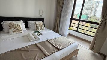 Quarto de hotel com uma cama grande, vista para a cidade pela janela e varanda com cortinas.