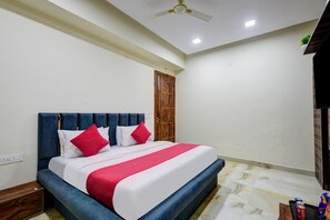 Quarto de hotel com cama, porta de madeira, ventilador de teto e piso de mármore.
