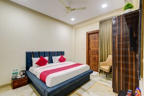 Quarto de hotel com cama, cadeira, porta de madeira e ventoinha no teto.