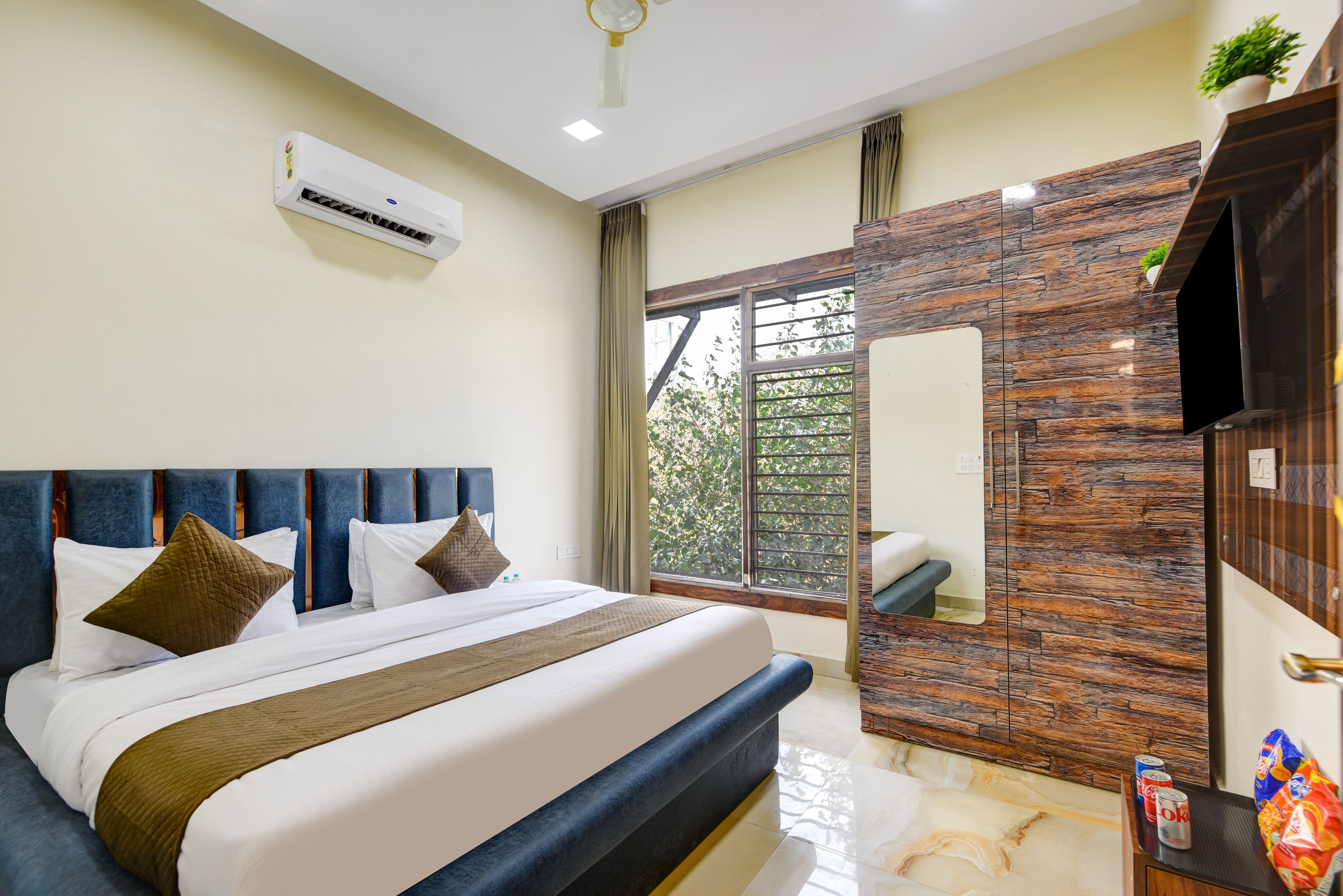 Quarto de hotel moderno com uma cama grande, ar condicionado integrado, banheiro com espelho e vista para o verde lá fora.