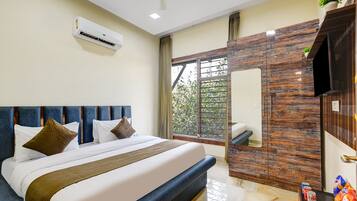 Quarto de hotel moderno com uma cama grande, ar condicionado integrado, banheiro com espelho e vista para o verde lá fora.