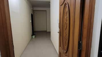 Um corredor com porta de madeira, lixeira e interruptor de luz na parede.
