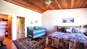 Quarto com teto de madeira, cama com roupa de cama estampada, tapete com estampas de animais e porta que dá para outro cômodo.