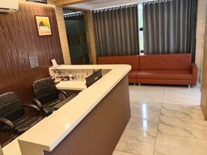 Uma área de recepção com balcão, cadeiras, sofá e uma janela com cortinas.