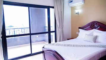 Quarto de hotel com uma grande porta de vidro deslizante para uma varanda, cama com roupa de cama branca e ar condicionado fixado na parede.