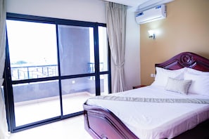 Quarto de hotel com uma grande porta de vidro deslizante para uma varanda, cama com roupa de cama branca e ar condicionado fixado na parede.